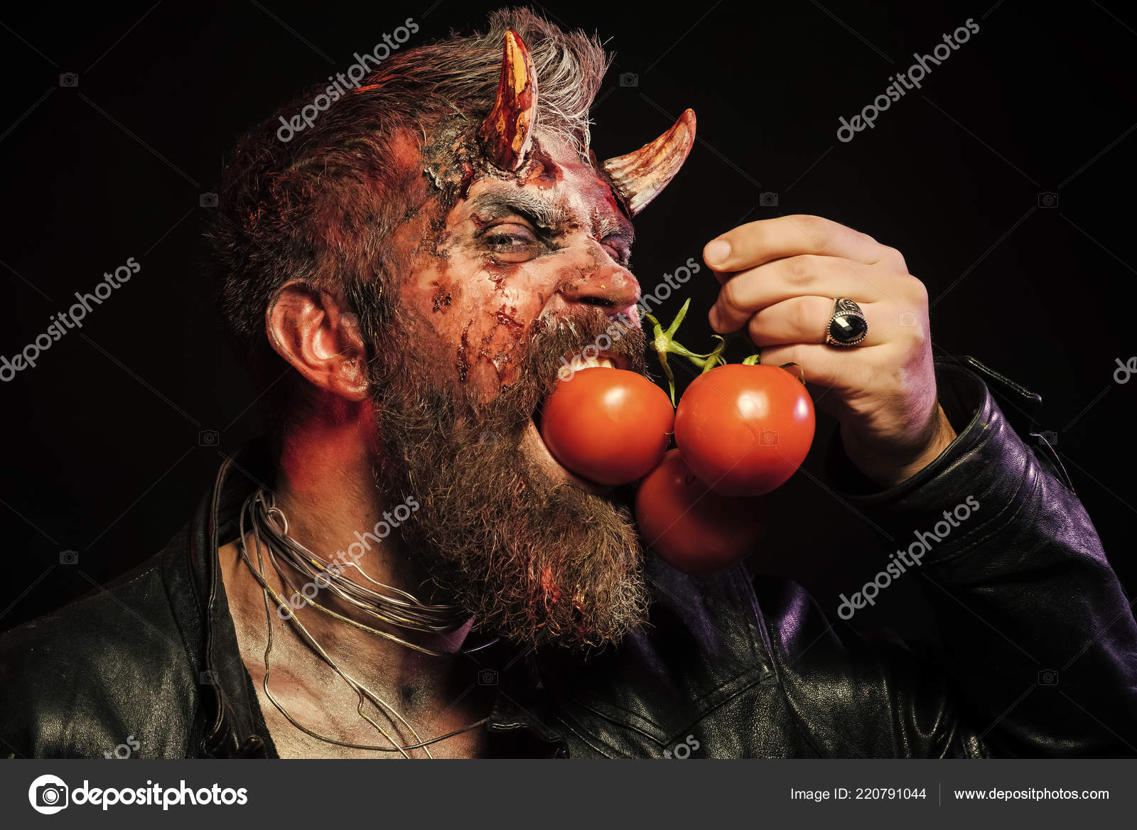 Halloween man with satan horns bite tomatoes on black background Stock ...