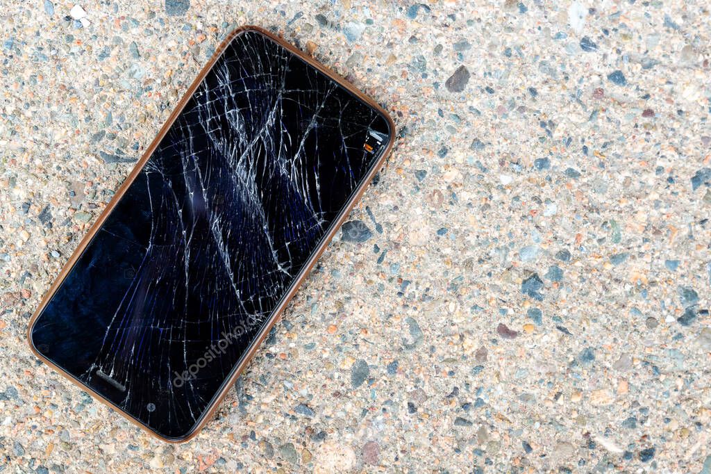 Un teléfono móvil destrozado y roto tirado en una acera de hormigón. La ...