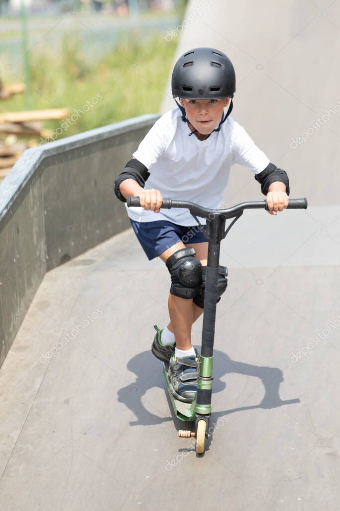 Un niño lindo monta una scooter en un parque de skate. Un joven atleta ...