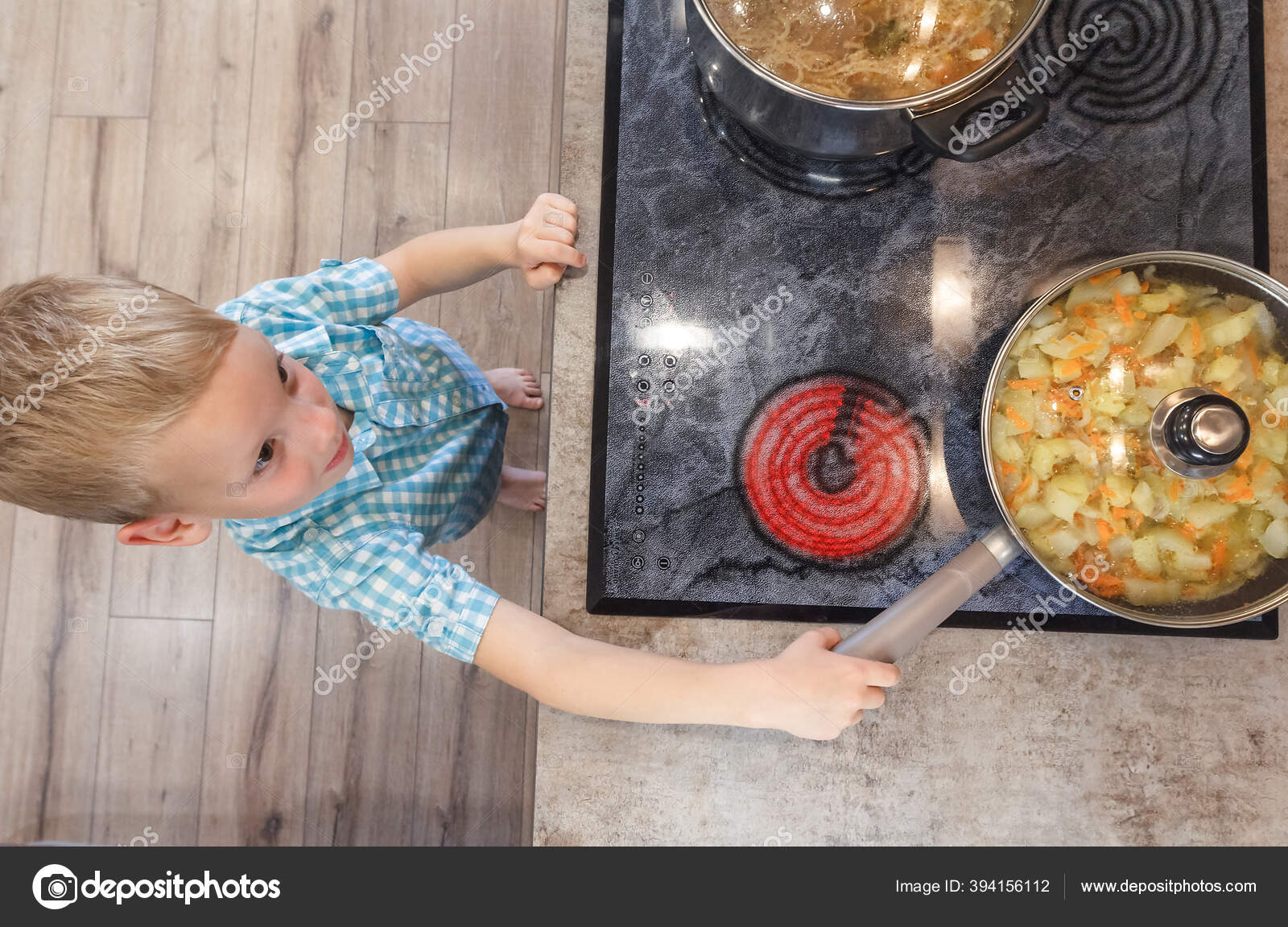 Little boy playing with pan on electric stove in the kitchen. Top view ...