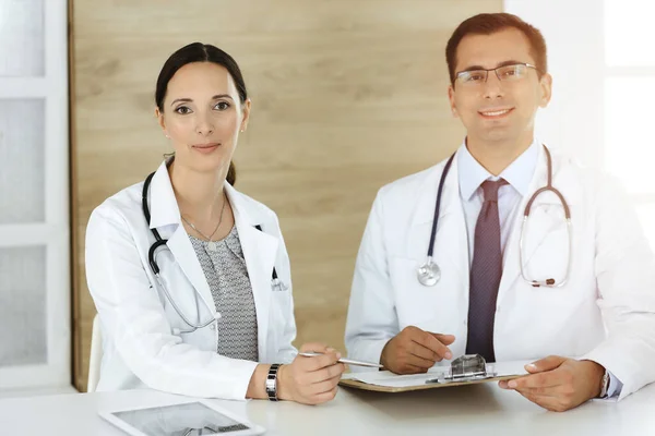 Two doctors discussing treatment problems while sitting at the desk in ...