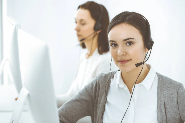 Call center. Casual dressed woman working in headset with diverse colleagues at office. Business ...