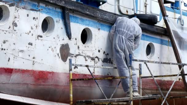 Working people tear off paint on metal in repairs process at shipyard ...