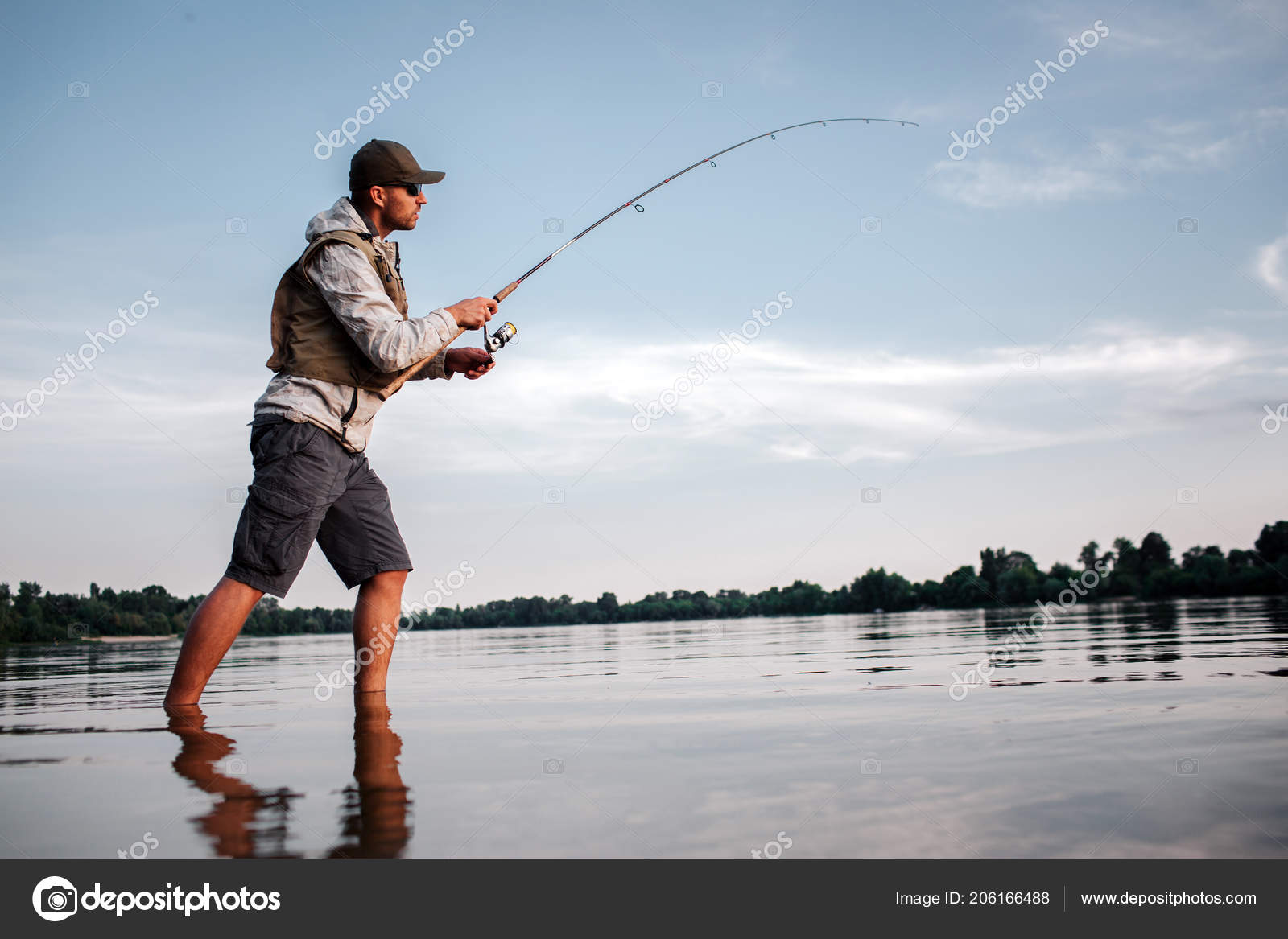 Active man is standing in shallow and fishing. He holds fly rod in ...