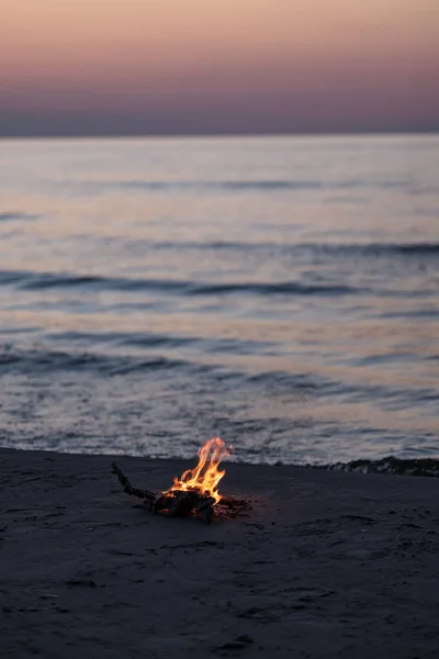 small fire burning on the sea shore at night with waves in background ...