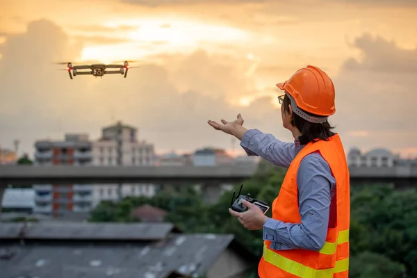 Young Asian engineer flying drone over construction site during sunset ...