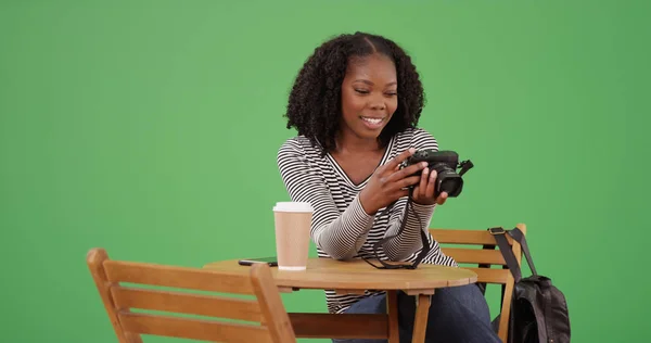 Young black female photographer with camera sitting at cafe on green ...