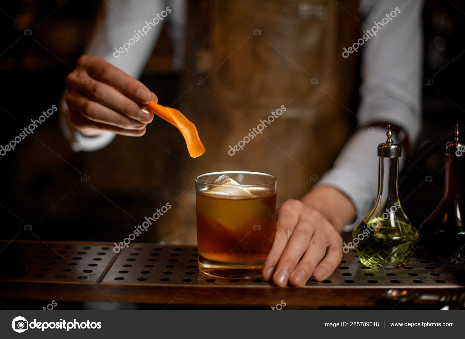 Professional male bartender adding an orange zest juice to a golden ...
