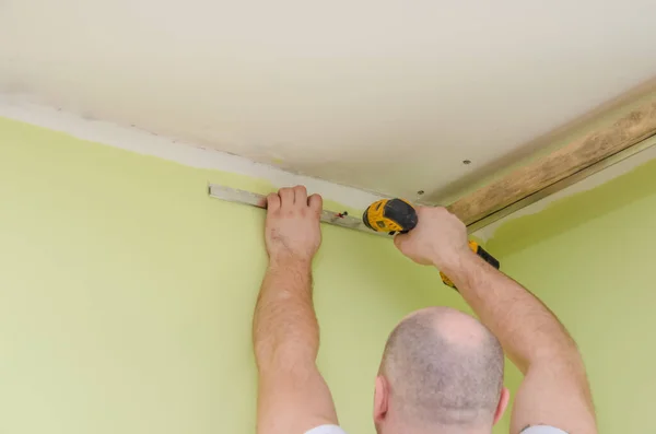 Fastening to the wall guide for stretch ceiling. Repairers make ...