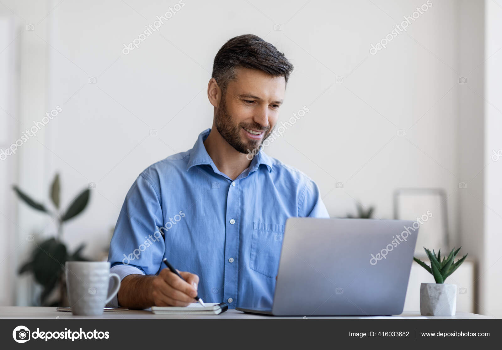 Millennial male entrepreneur using laptop and taking notes at workplace ...