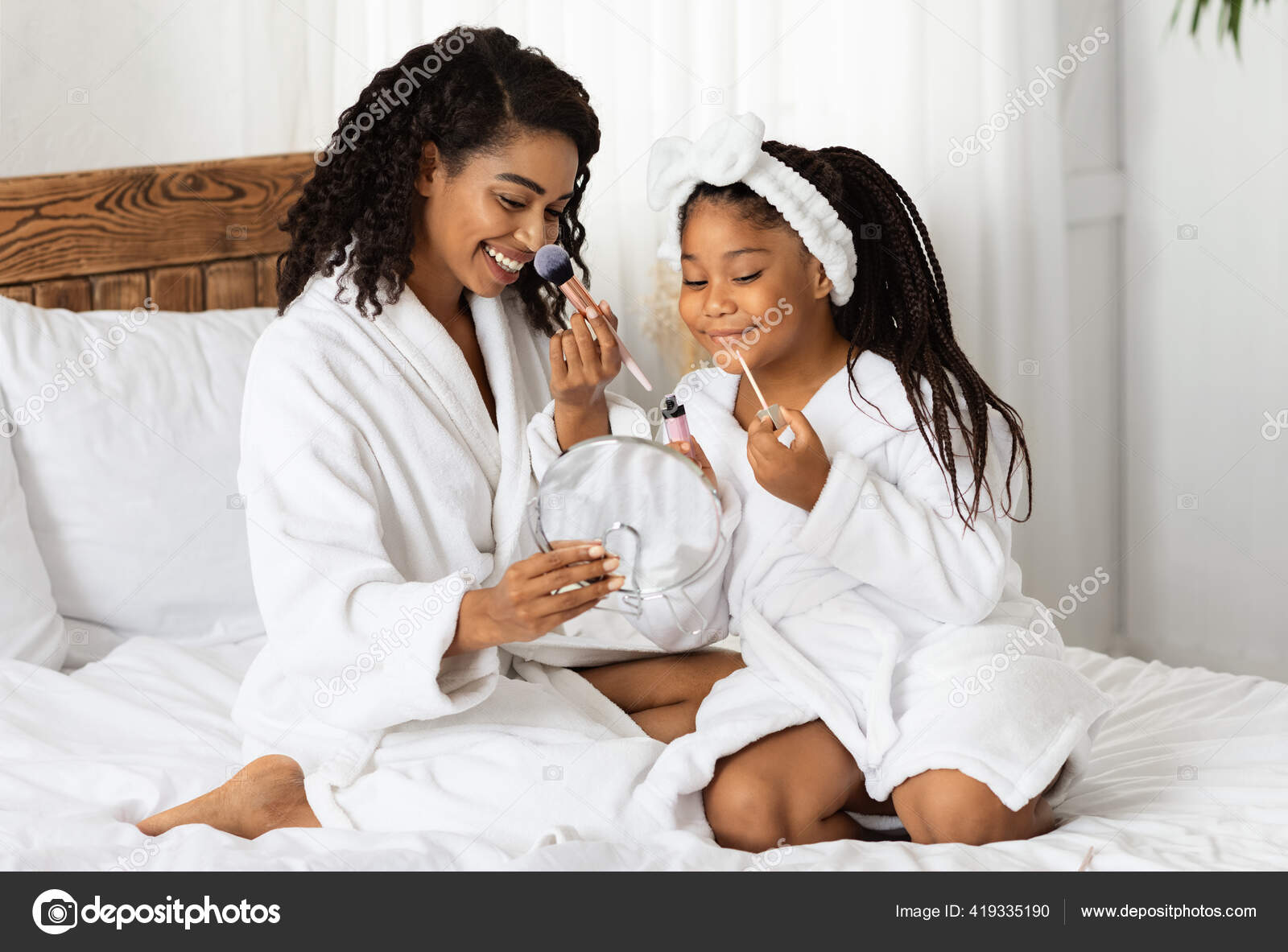 Beautiful happy black mother and little daughter in bathrobes applying makeup together Stock ...