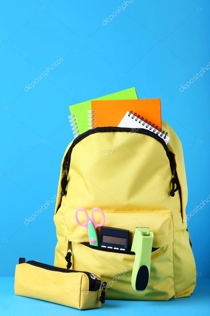 Mochila amarilla con útiles escolares sobre fondo azul 2022