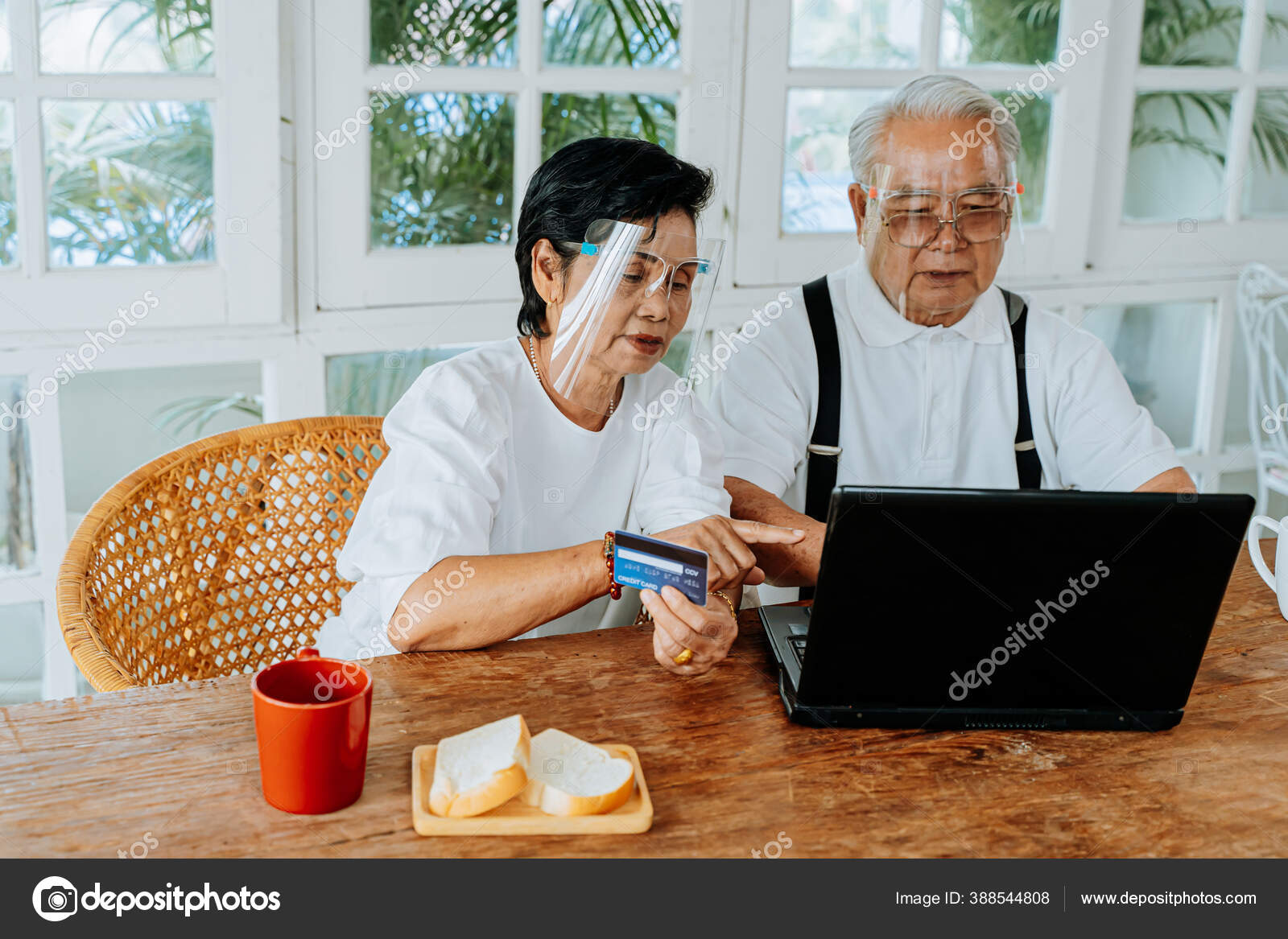Elderly Asian couple in personal protective face shield sitting at ...