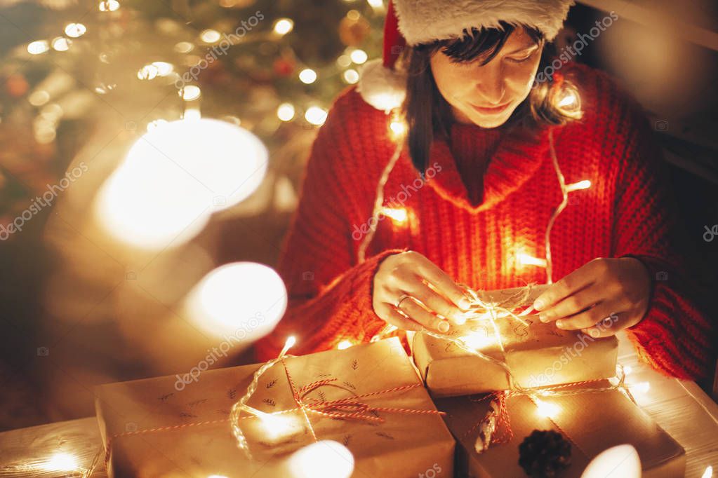 niña en sombrero de santa y suéter rojo envolviendo regalos de Navidad ...
