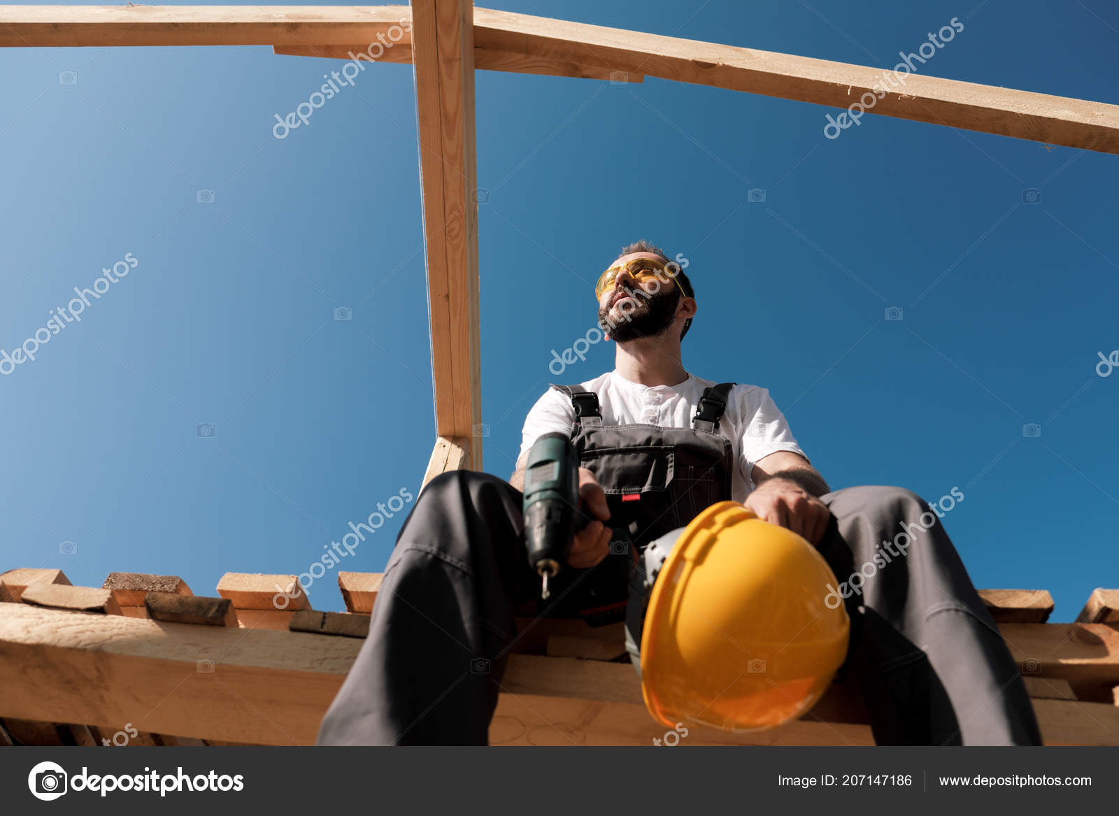 The man builder sits on the edge of the roof of the frame house, in a ...