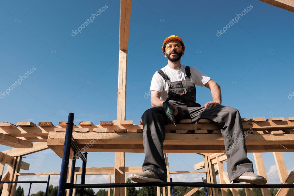 El hombre constructor se sienta en el borde del techo de la casa de ...