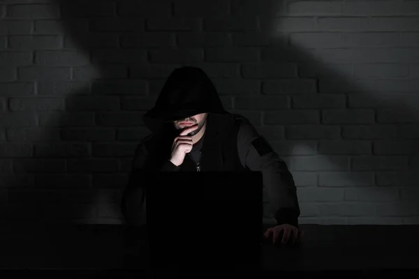 Hacker in black mask and hood at the table - Stock Image - Everypixel