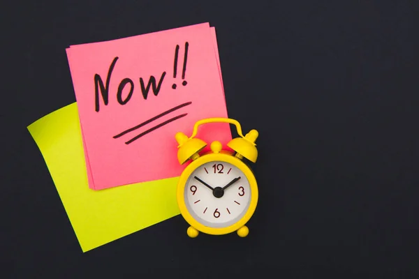 Sticker with handwriting the word NOW on alarm clock on dark blue ...