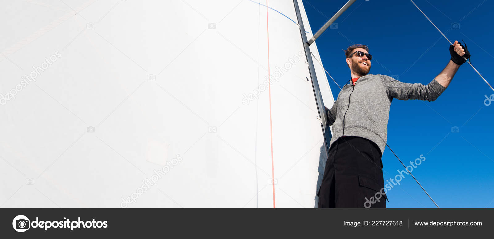 Yacht captain with a beard stands on sail boom on a sailing yacht ...