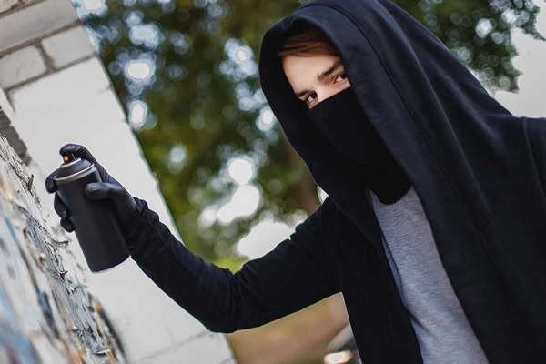 Hooded man in mask drawing graffiti by spray can with paint. Graffiti ...