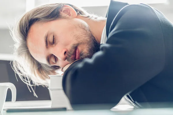 Handsome young man sleeping on pile of books at work desk. Coffe ...