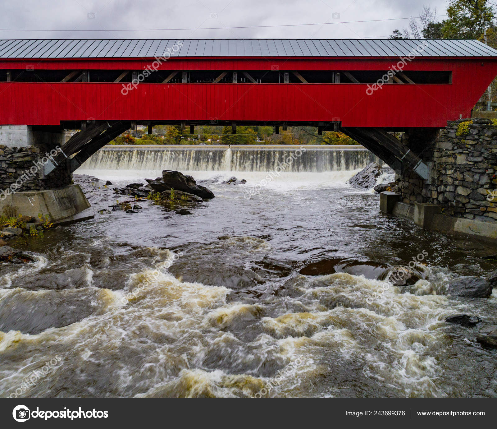 A red covered bridge first built in 1883 spans a rapidly flowing river ...