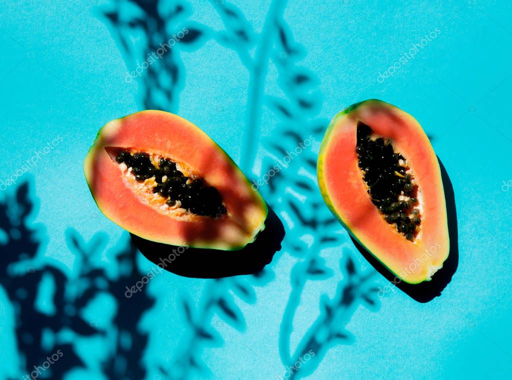 Papaya recién cortada con cenizas y sombras de ramas sobre fondo azul 2023