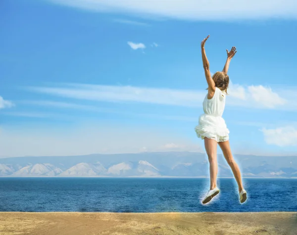free woman. back view of jumping woman against blue sky and snowy ...