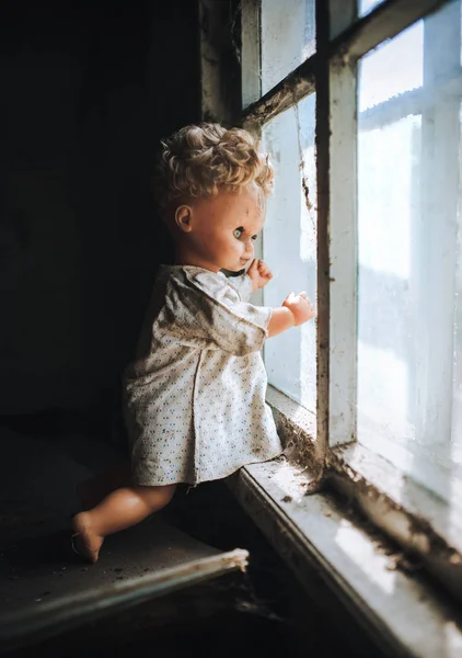 Abandoned dirty doll looking through window of old house - Stock Image ...