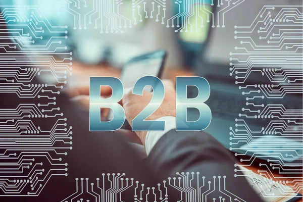 Circuit board on the background of a man working on a laptop and holding a smartphone in his ...