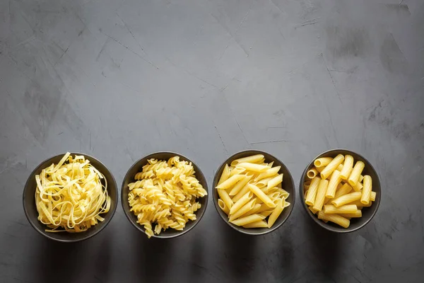 Different types of pasta in wooden bowls on a gray concrete back ...