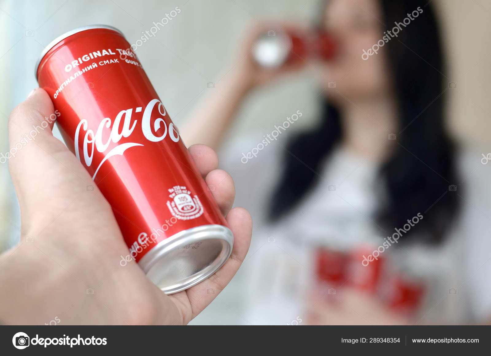 Brunette woman drinks Coca-Cola drink in garage interior and male hand ...