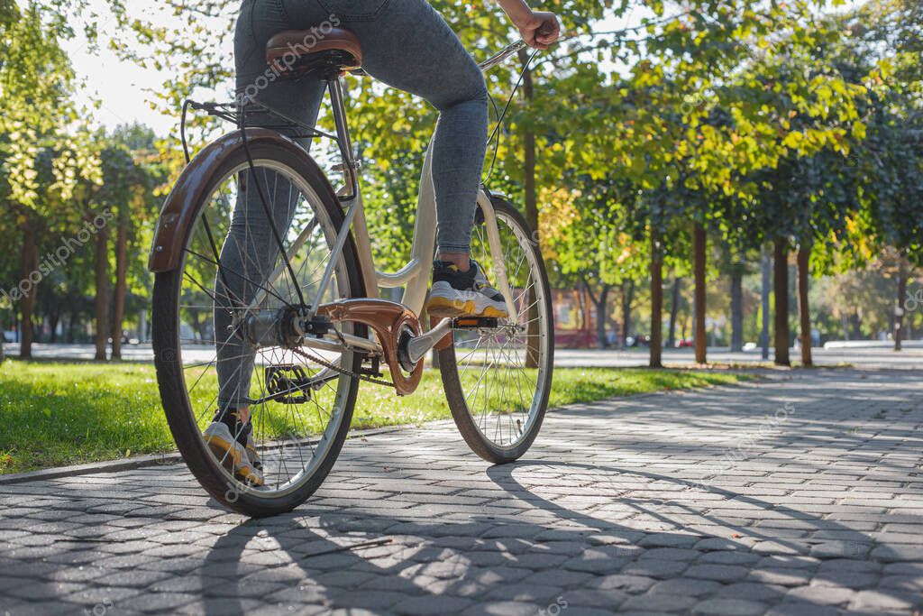 Una chica en jeans y zapatillas de deporte se sienta en una bicicleta ...