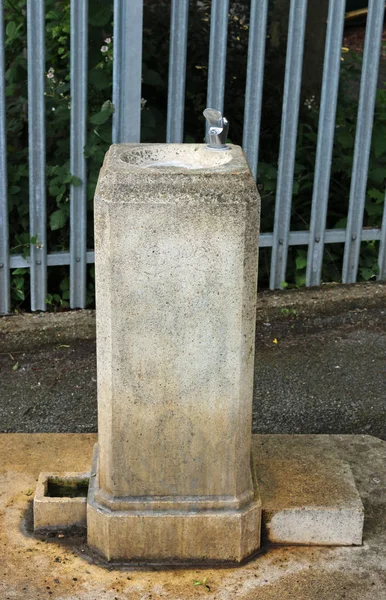 Concrete drinking fountain on a plinth in a park with a grey metal ...