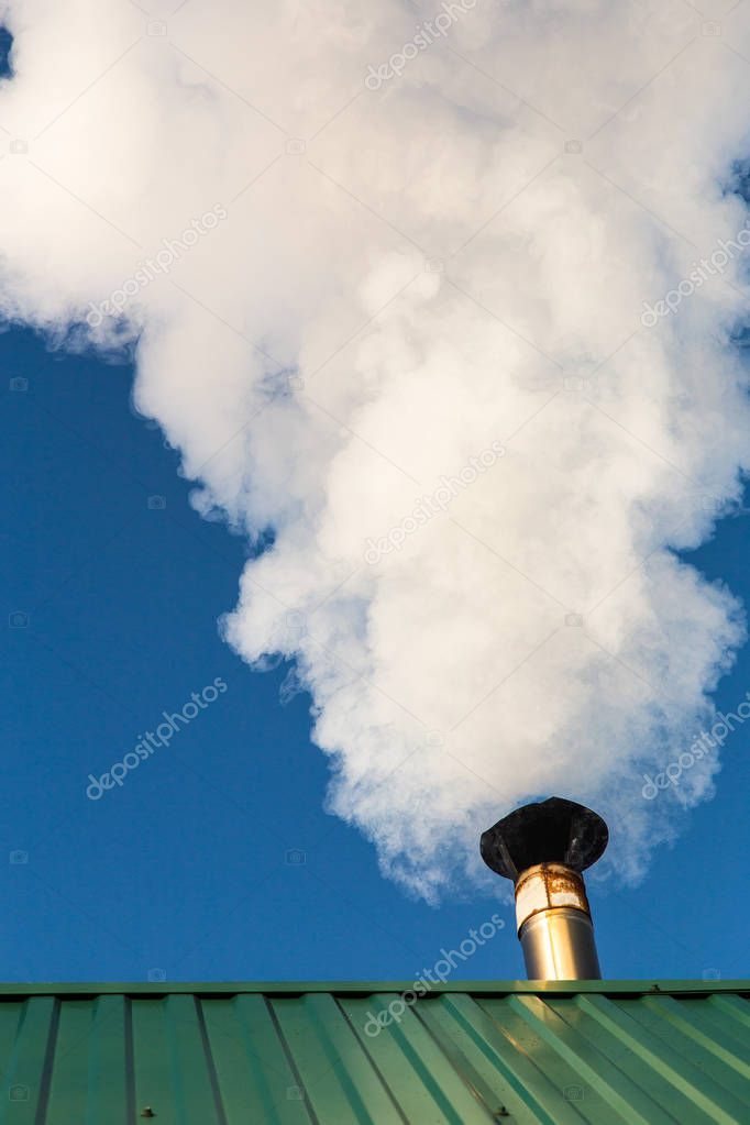 El humo viene de la chimenea de la casa contra el cielo azul. La tubería en el techo. Chimenea ...
