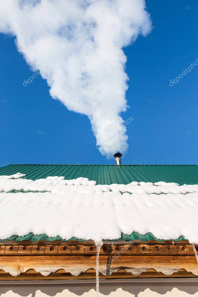 El humo viene de la chimenea de la casa contra el cielo azul. La tubería en el techo. Chimenea ...