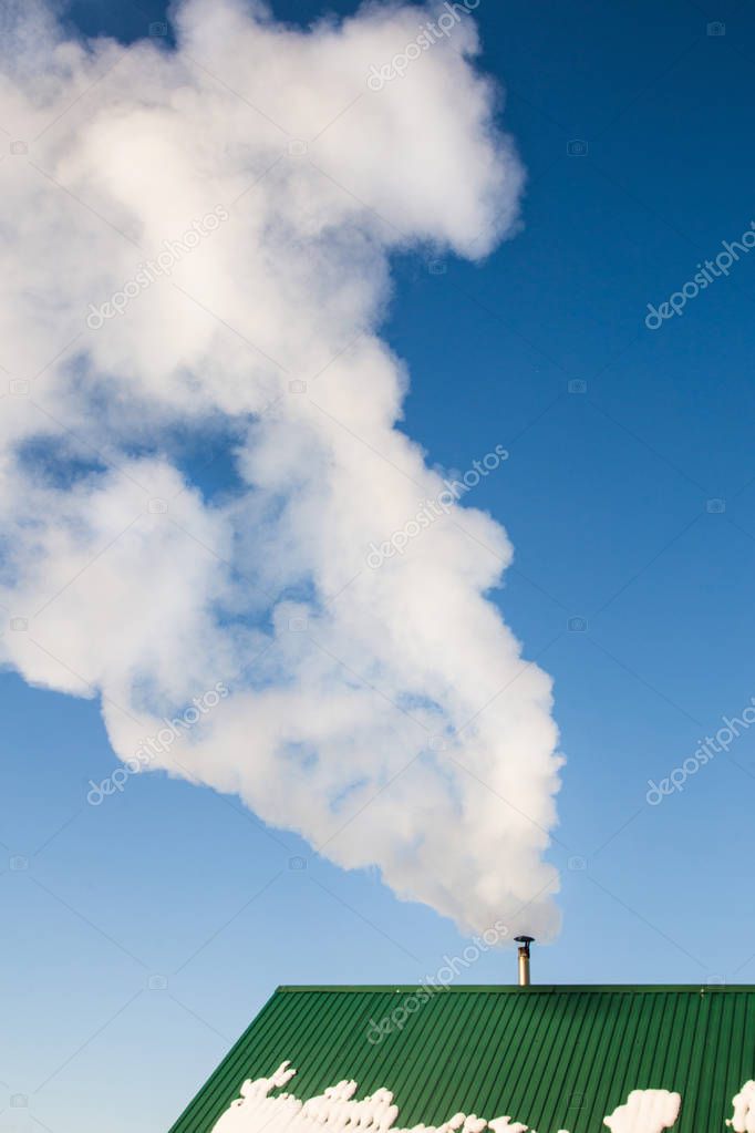 El humo viene de la chimenea de la casa contra el cielo azul. La tubería en el techo. Chimenea ...