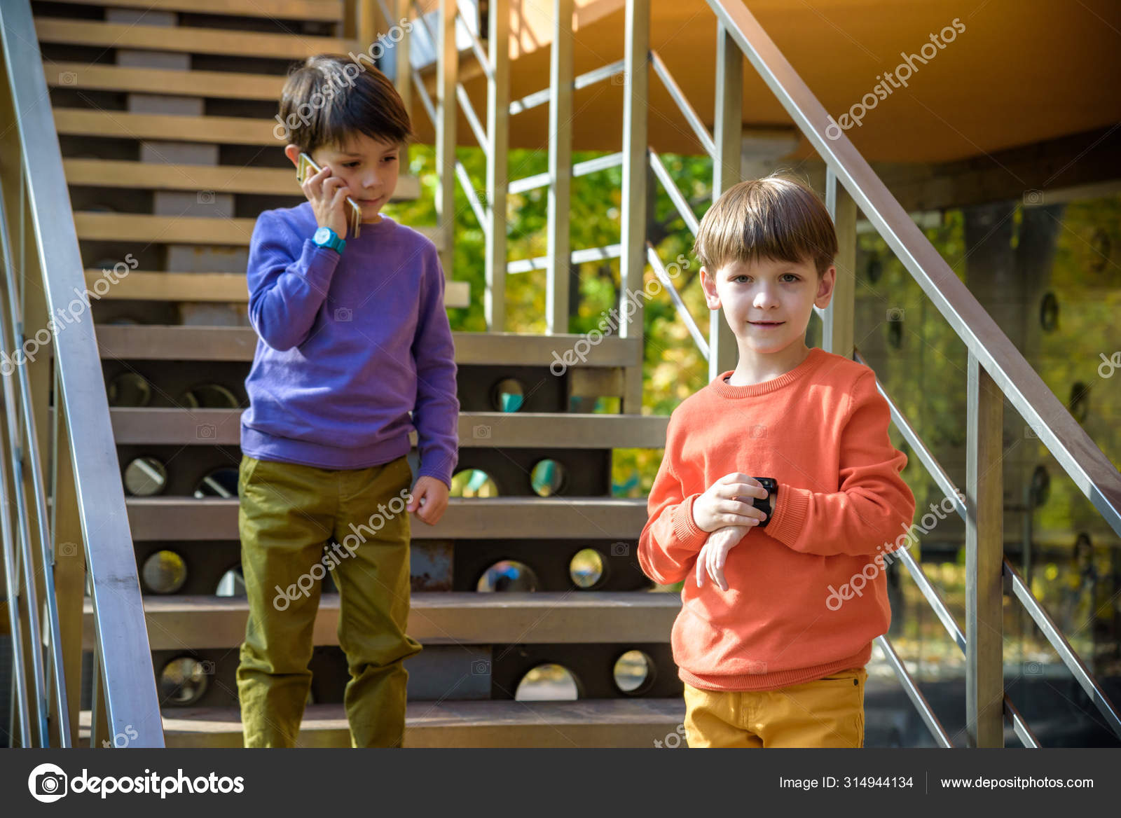 Two friends calling each other while standing on stairs outdoor. One ...