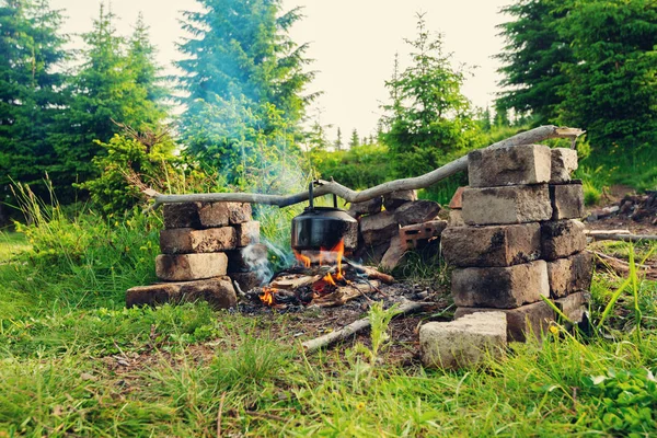Old small kettle is heated on a bonfire on a green mountain meadow ...