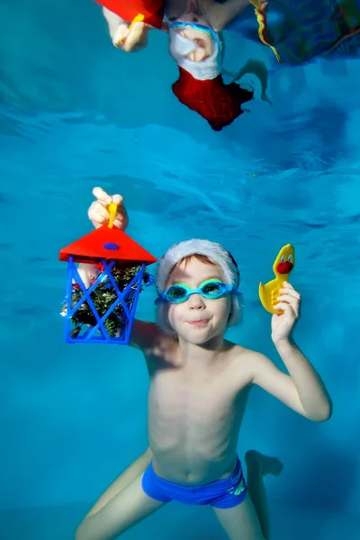 Happy little boy swims underwater in Santa's red hat and swimming ...
