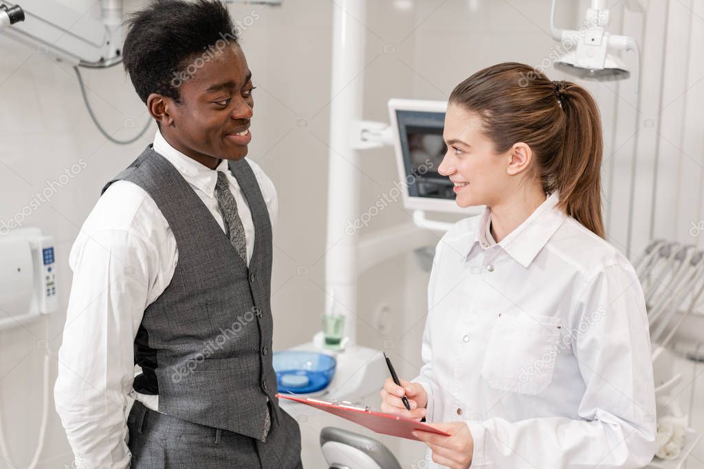 Mujer joven dentista hace un diagn stico y registra las recomendaciones. Paciente masculino ...