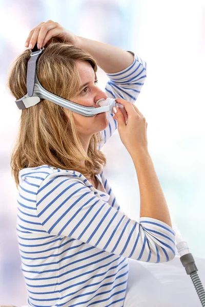 Woman trying to wear CPAP mask, sleep apnea therapy.Profile view ...