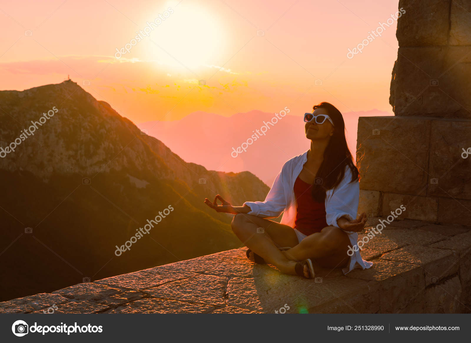 Woman siting at the edge with beautiful view of sunset over mountains ...