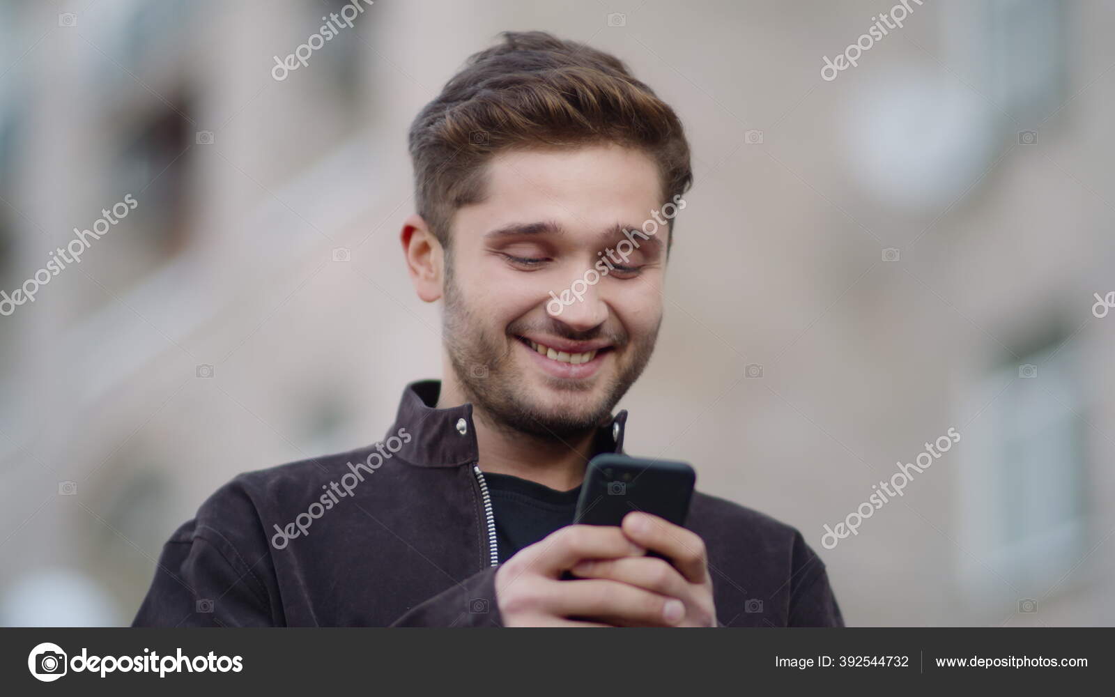 Smiling guy using phone on street. Happy man looking phone screen ...