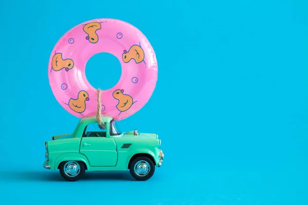 Car toy and inflatable pool float against blue background on the road ...