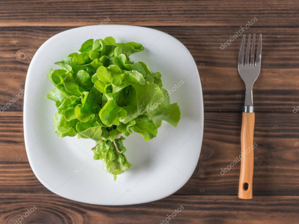 Un ramo de lechuga en un plato blanco y un tenedor en una mesa de ...