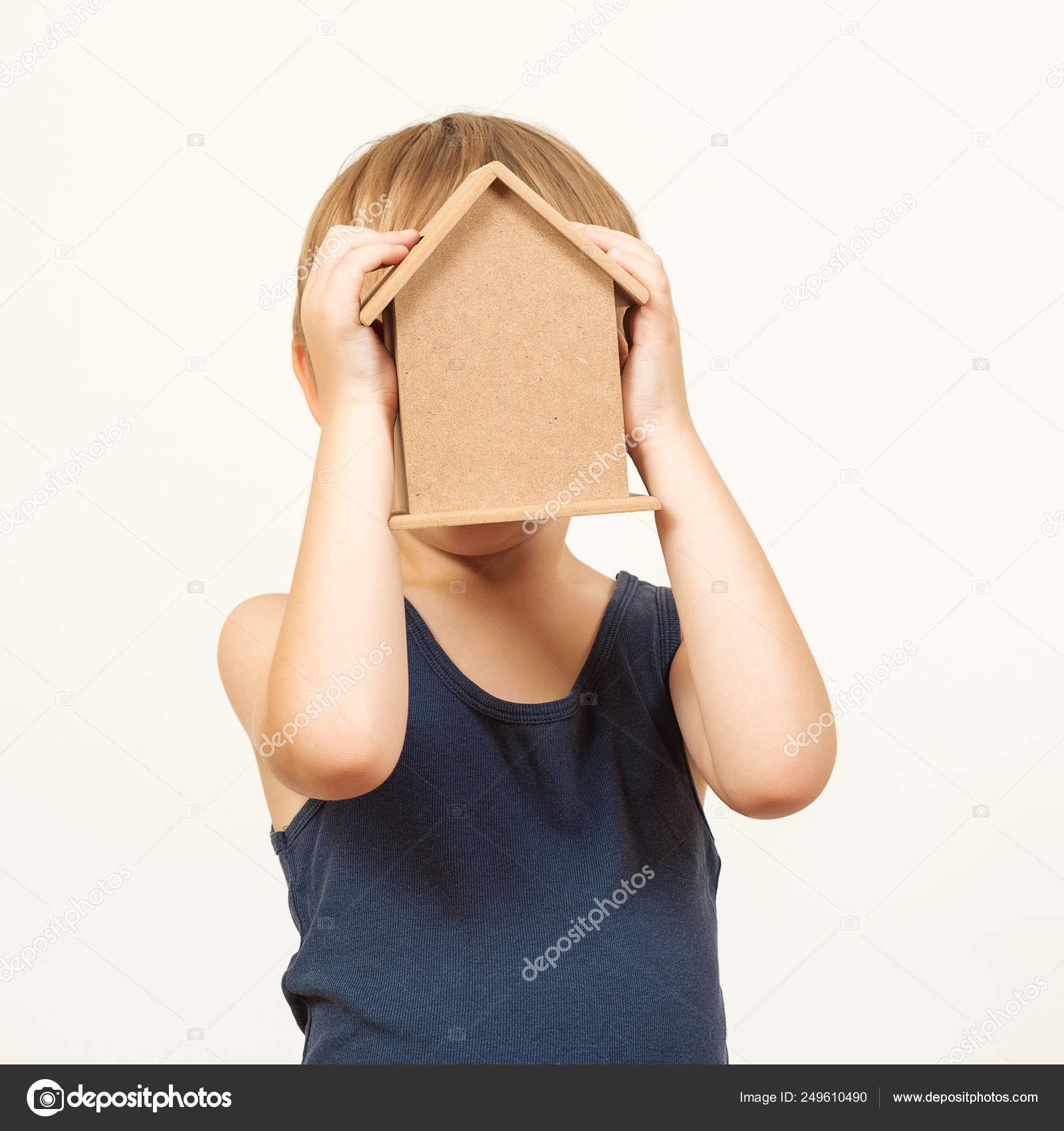 Happy kid hid his face behind small house toy. Dreaming about own home ...