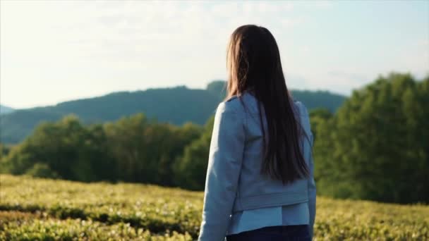 Brunette girl is walking calmly between green bushes in a garden near ...