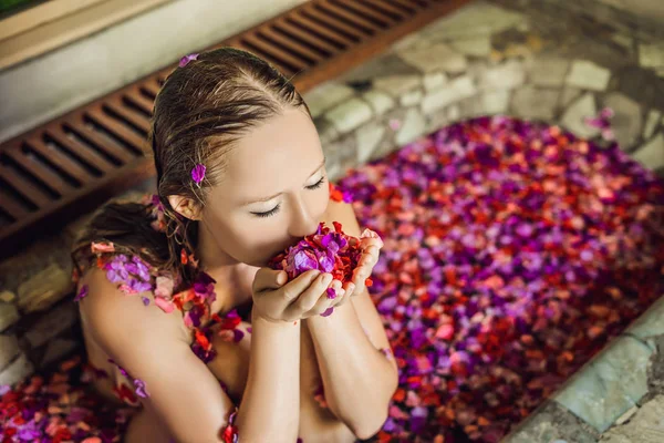 Young woman enjoying spa bath with petals of tropical flowers and aroma oil. - Stock Image ...