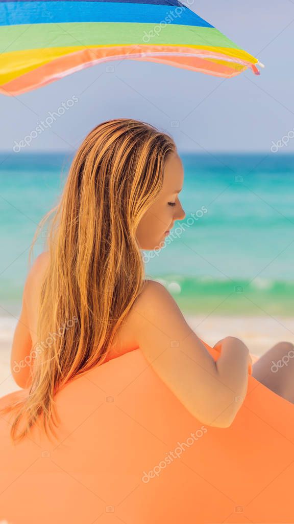 Retrato de estilo de vida de verano de una chica bonita sentada en el sofá inflable naranja en ...